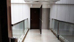 Um corredor com piso de azulejos, guarda-corpos de vidro e uma porta no final.