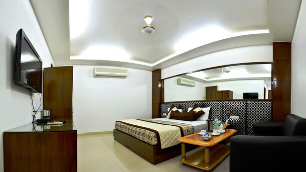 Quarto de hotel moderno com cama, escrivaninha, cadeira, televisão e espelho.