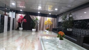 Um hall amplo com piso de mármore, uma mesa de vidro com arranjos florais e um sofá de couro.