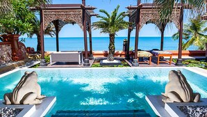 Piscina com duas estátuas de sapo, uma pérgula e vista para o oceano.