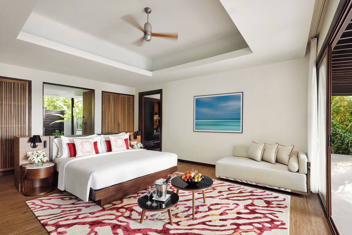 Quarto moderno com cama, mesas de cabeceira, um sofá, ventilador de teto, uma janela grande e uma pintura.