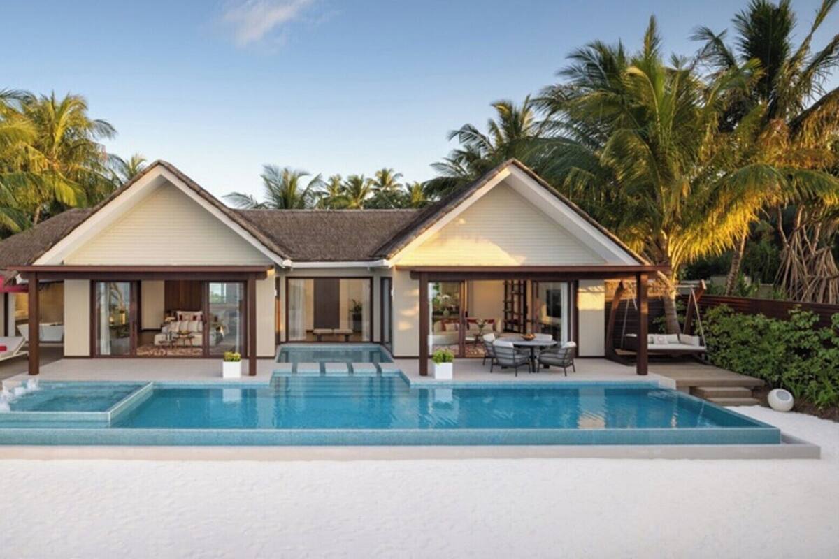 Resort de dois andares com uma grande piscina, áreas de estar ao ar livre e palmeiras.
