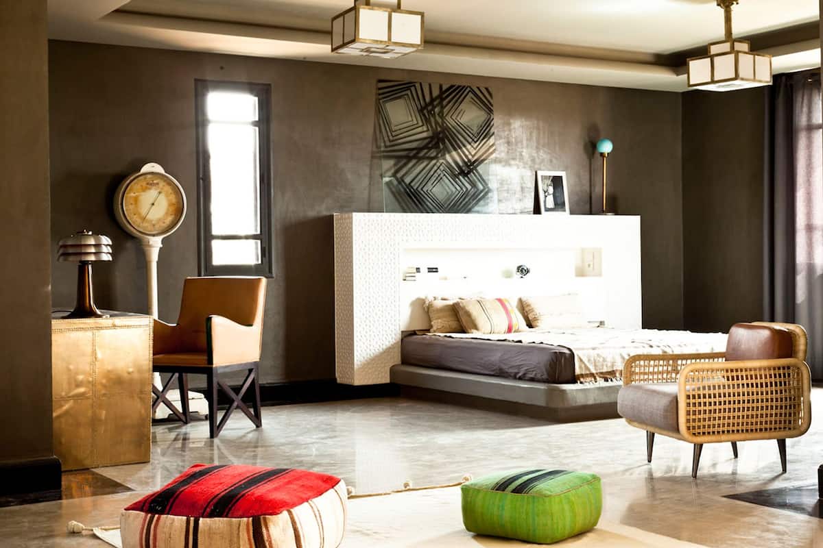 Um quarto moderno com uma cama, uma cadeira, um banquinho e um relógio de parede.
