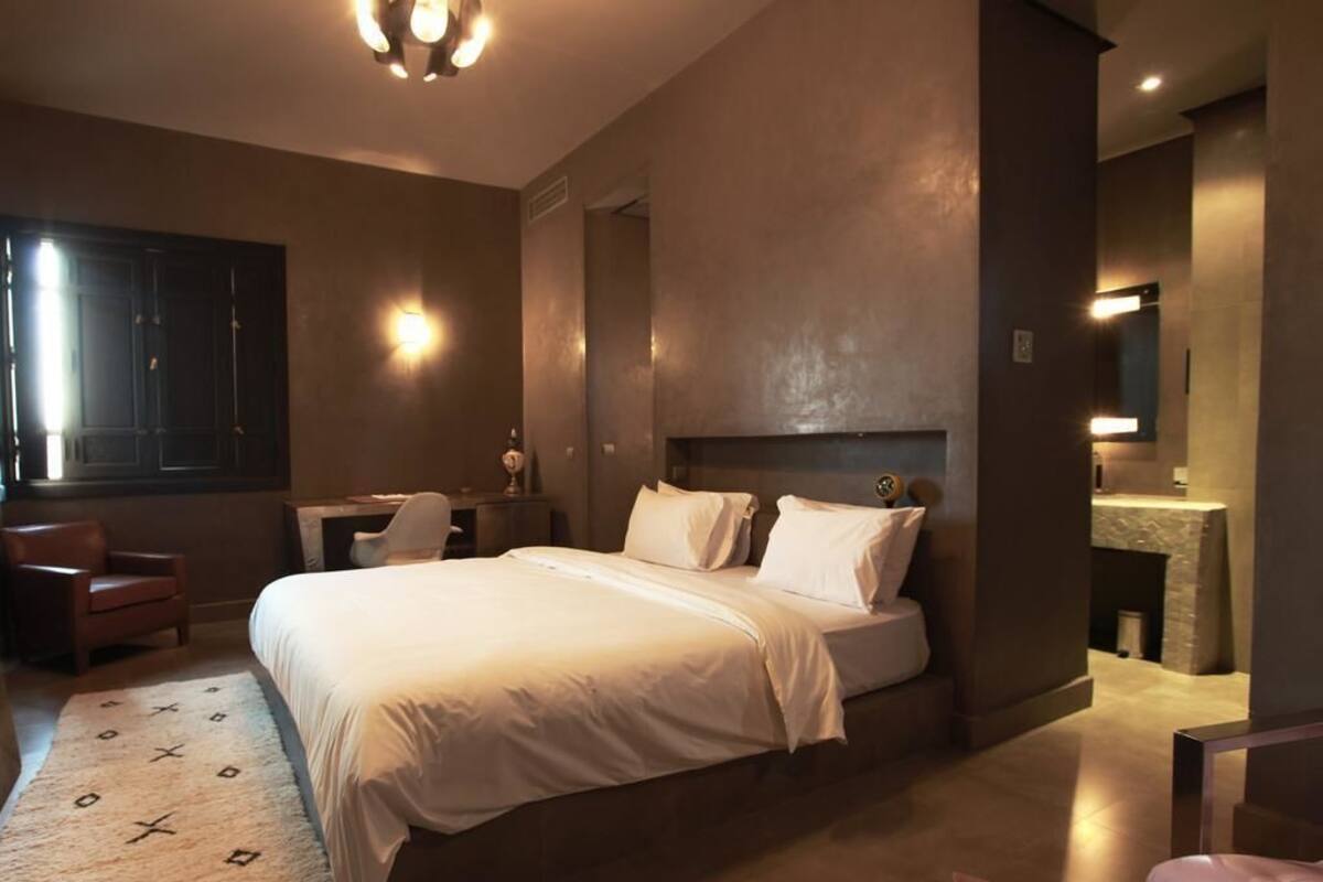 Quarto moderno com uma cama grande, uma escrivaninha e um banheiro visível ao fundo.