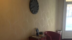 Um quarto com duas cadeiras vermelhas, uma mesinha com uma planta e um relógio de parede.