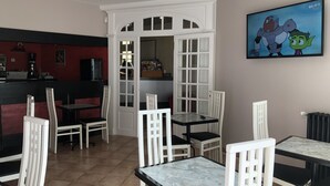 Um restaurante com mesas e cadeiras brancas e pretas, uma área de cozinha e uma ilustração de desenho animado na parede.