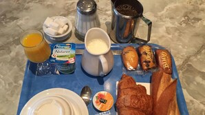 Bandeja de café da manhã com croissants, doces, suco de laranja, café, cubos de açúcar e acompanhamentos.