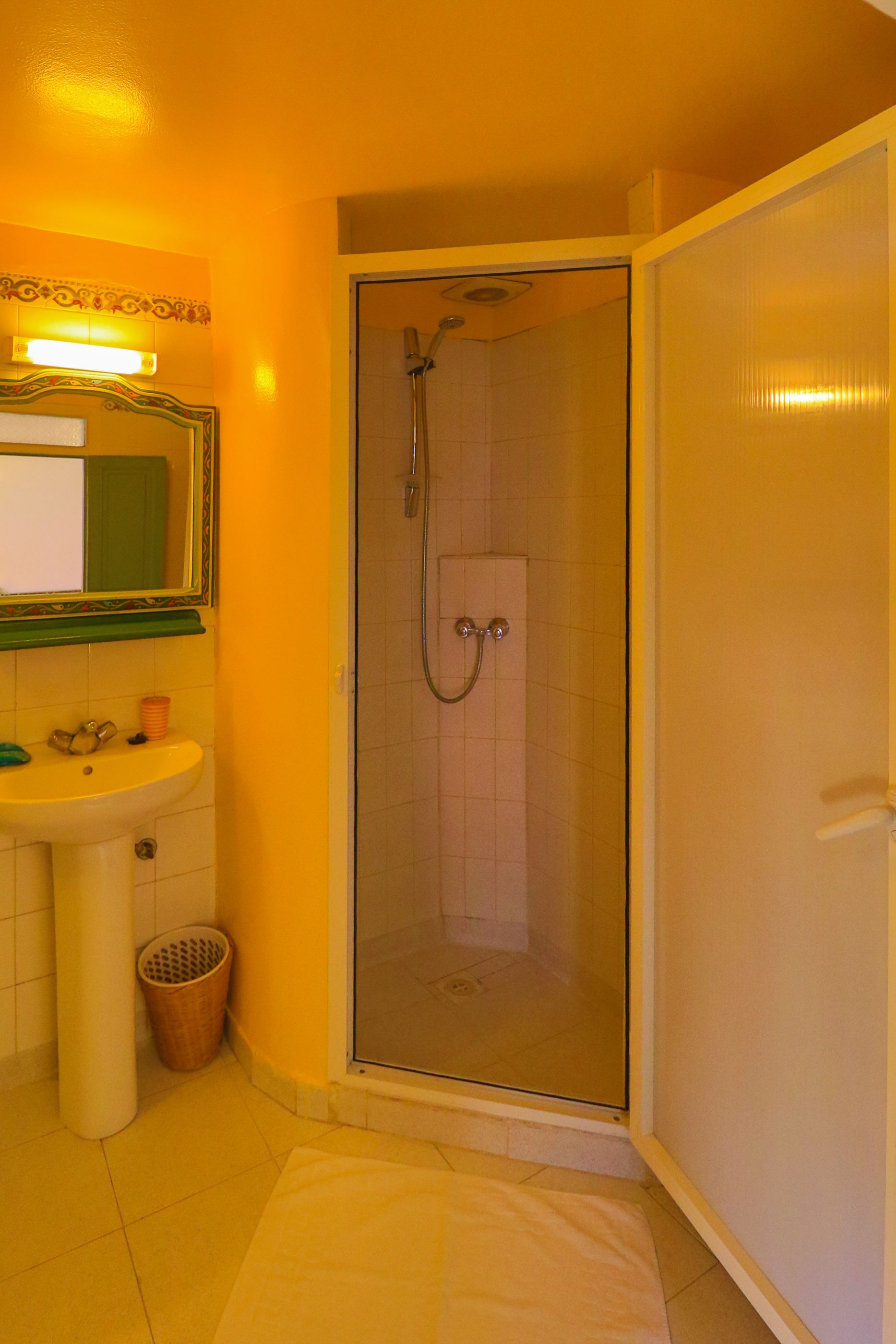 Casa de banho com chuveiro envolto em vidro, lavatório e espelho.