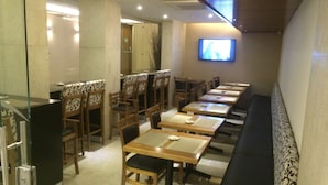 Um restaurante com mesas compridas e cabines, cadeiras de madeira e uma tela de televisão na parede.