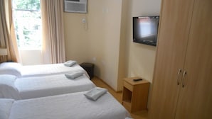 Quarto de hotel com duas camas, televisão, ar condicionado e uma pequena mesa de madeira.