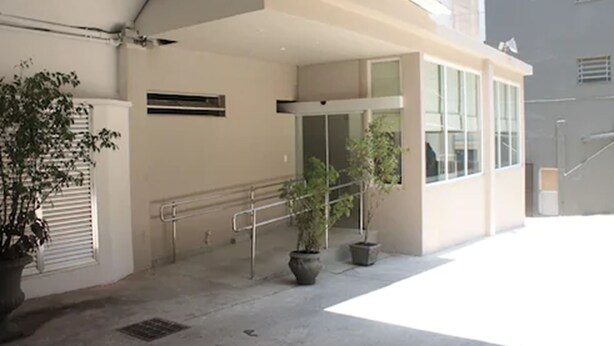 Entrada de um edifício com porta de vidro, plantas em vasos e corrimão de metal.