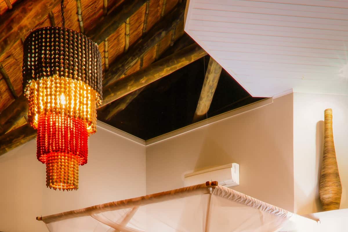 Uma cama de dossel com cortina, um banco vermelho, um tapete tecido e teto de madeira.