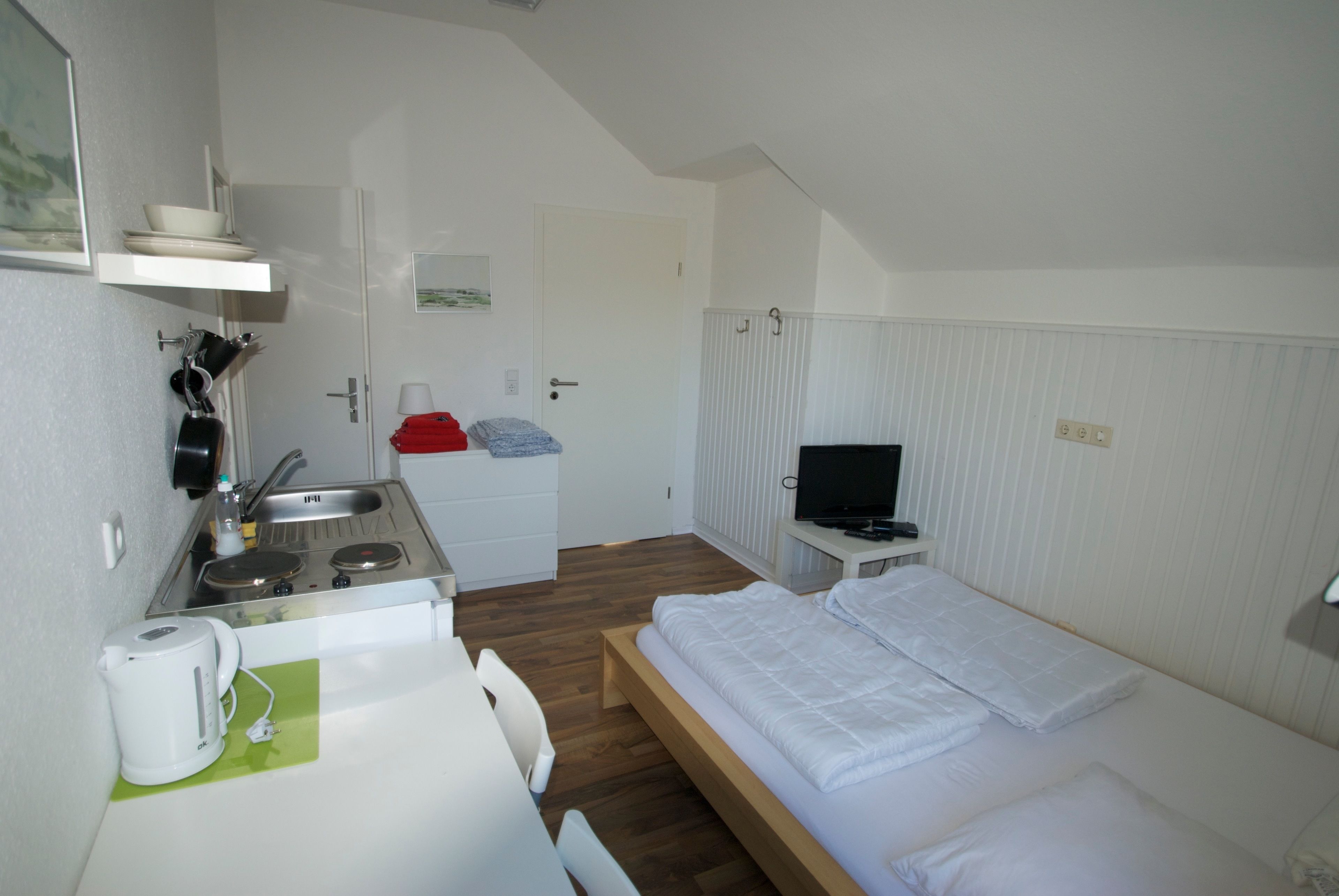 Quarto de hotel pequeno com cozinha compacta, uma cama, televisão e radiador.