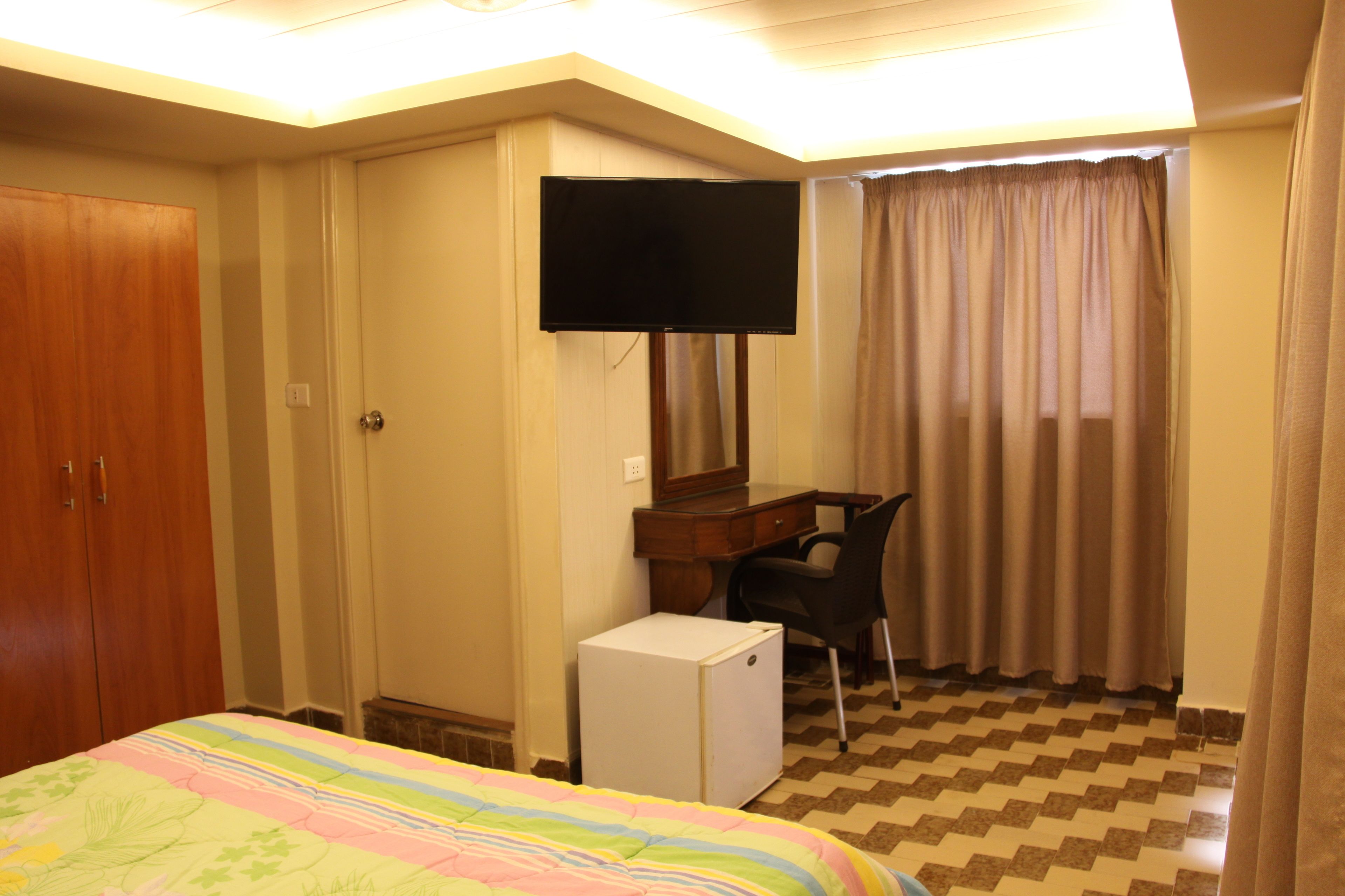 Quarto de hotel com cama, escrivaninha, televisão, frigorífico e guarda-roupa.