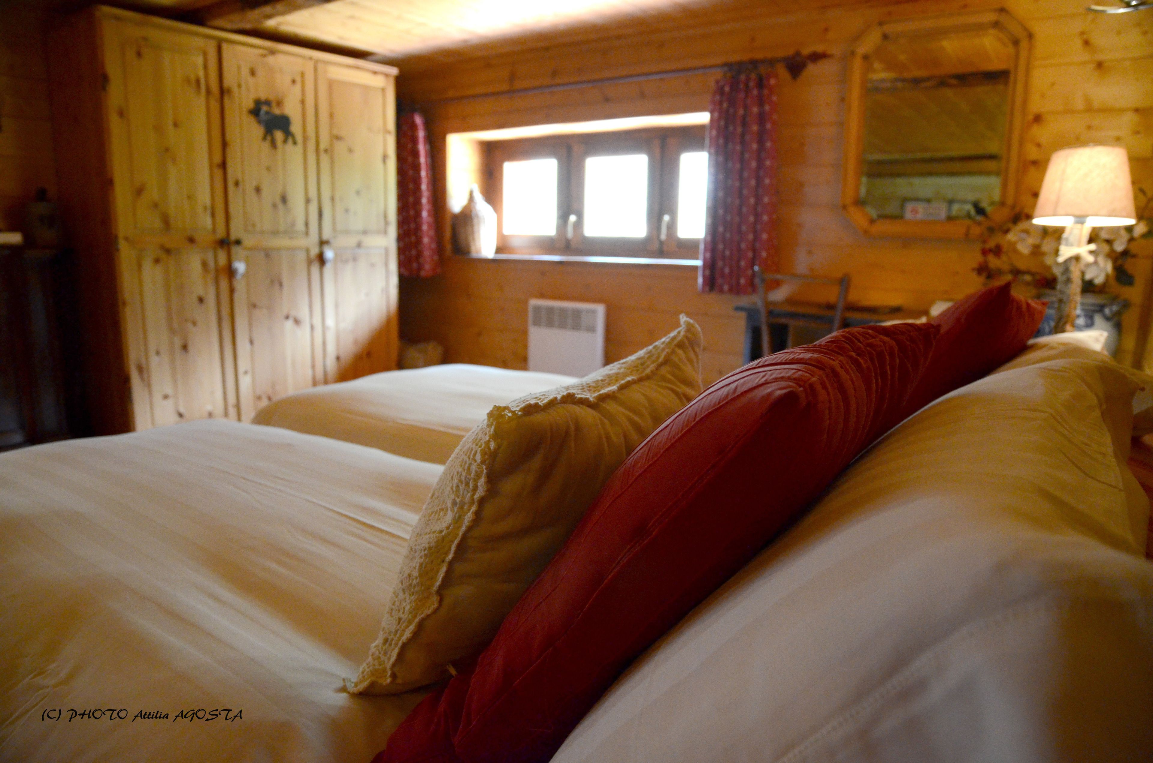 Quarto de cabana de madeira com cama, guarda-roupa e janela com cortinas.