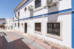 Um edifício branco com detalhes azuis, aparelhos de ar condicionado e calçada vermelha.
