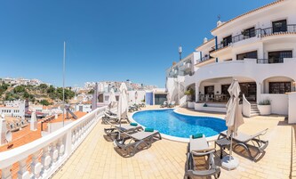 Piscina no terraço com espreguiçadeiras e vista da cidade.