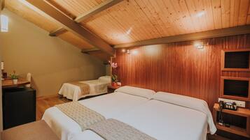 Quarto de hotel com teto de madeira, duas camas, uma pequena escrivaninha com uma planta e uma televisão sobre uma estante de madeira.