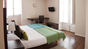 Quarto de hotel com cama, escrivaninha, cadeira, televisão e janelas amplas.