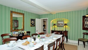Uma sala de jantar com uma mesa comprida posta para refeição, rodeada por cadeiras de madeira.