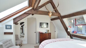Quarto com teto inclinado, uma cama, cômoda, cadeira e espelho.