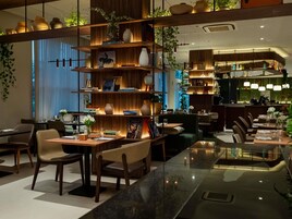 Interior moderno de restaurante com prateleiras de madeira, mesas, cadeiras e iluminação ambiente.