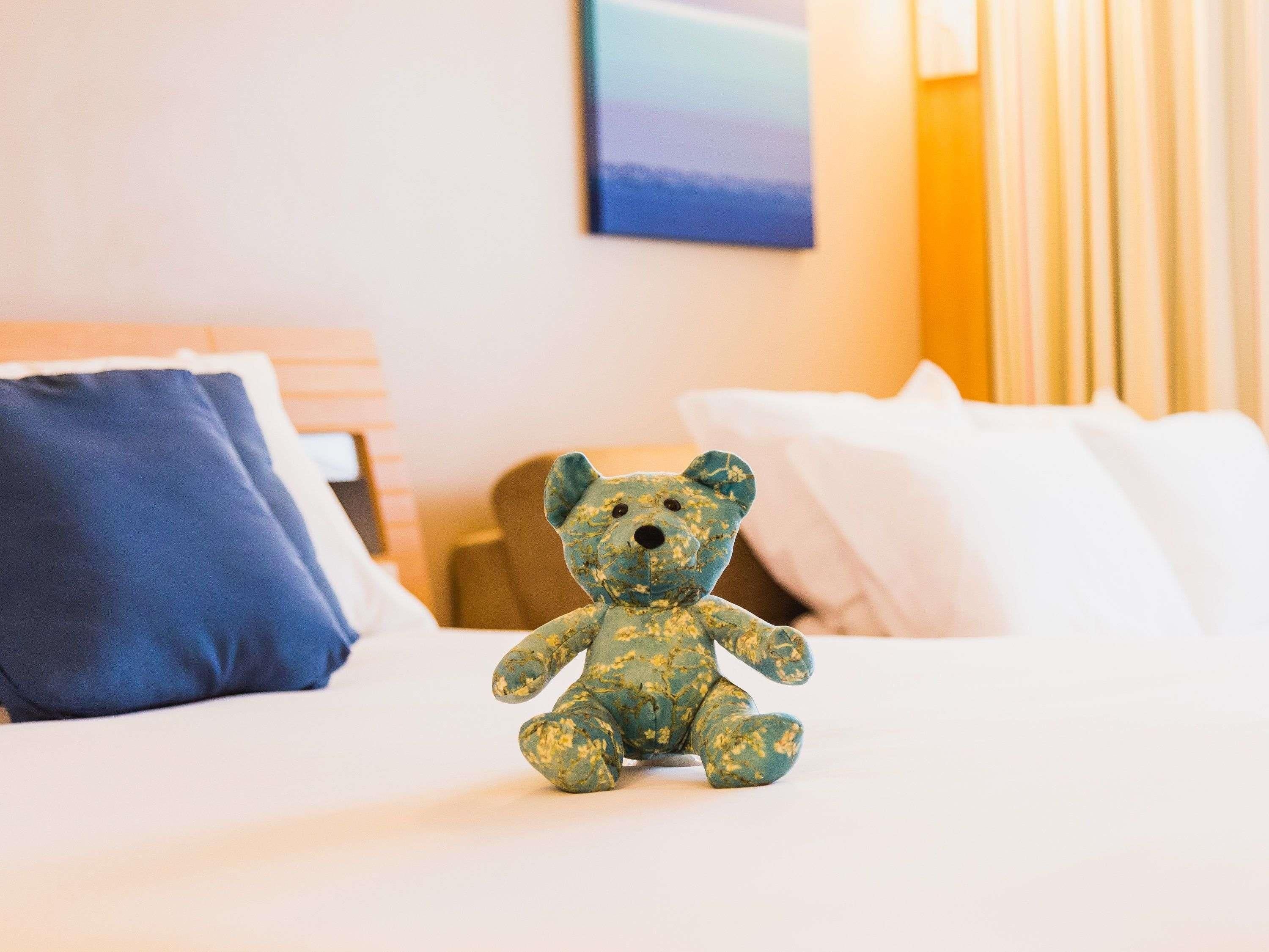 Uma cama com um travesseiro azul, um travesseiro branco e um pequeno urso de pelúcia azul.