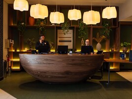 Uma receção com acabamento em madeira, vários postos de computador e luminárias pendentes.