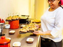 Uma pessoa segurando uma bandeja de aperitivos em uma mesa de buffet com diversos alimentos e recipientes.