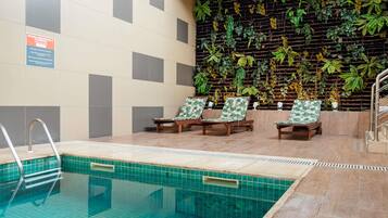 Piscina interna com chão e paredes revestidos, rodeada por cadeiras de lounge com estampas tropicais.