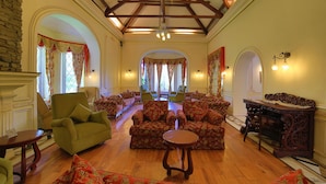 Uma sala ampla com piso de madeira, sofás estofados em tons de verde e vermelho, uma mesa de centro de madeira e uma lareira.