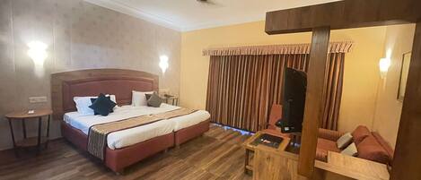 Quarto de hotel com uma cama grande, uma mesa de cabeceira de madeira, um ventilador de teto e vista para o exterior através de cortinas.