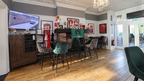 Uma área de refeições com piso de madeira, banquetas de bar, uma televisão e itens de coleção esportiva emoldurados na parede.