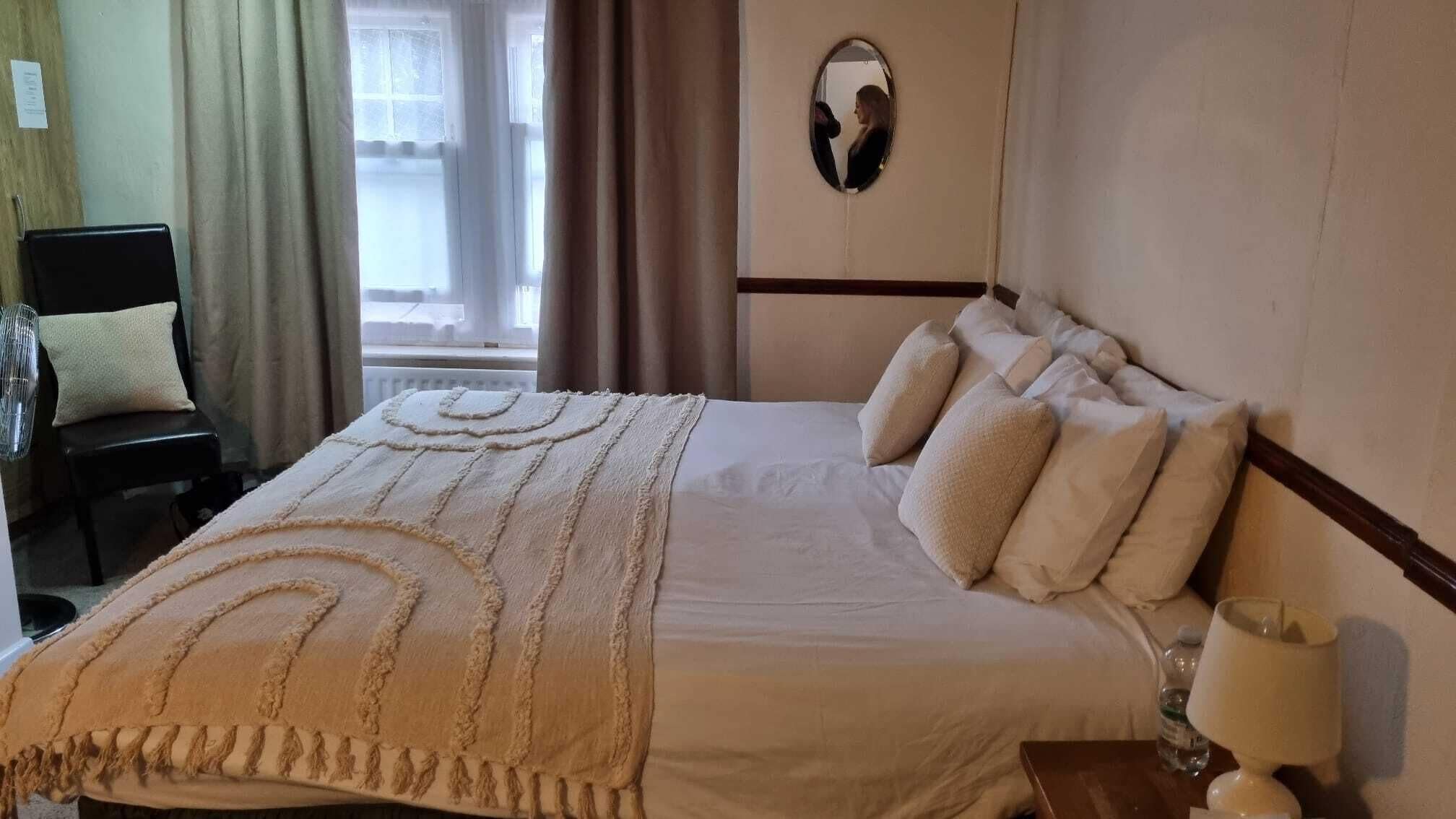 Uma cama bem arrumada com uma manta decorativa, uma luminária de cabeceira e uma cadeira com almofada.