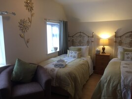 Um quarto com duas camas, uma mesa de cabeceira com abajur, uma cadeira e decoração na parede.
