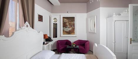 Quarto com uma cama grande, uma escrivaninha com luminária, duas cadeiras, um candelabro e um quadro na parede.