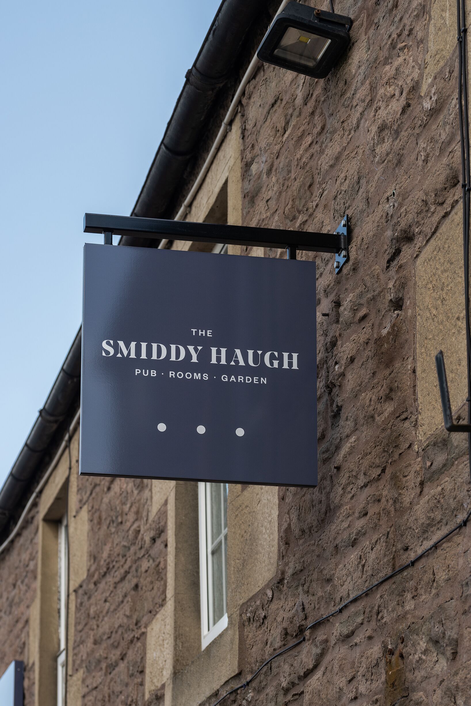 Placa com o nome 'The Smiddy Haugh Pub, Rooms, Garden' fixada em um edifício.