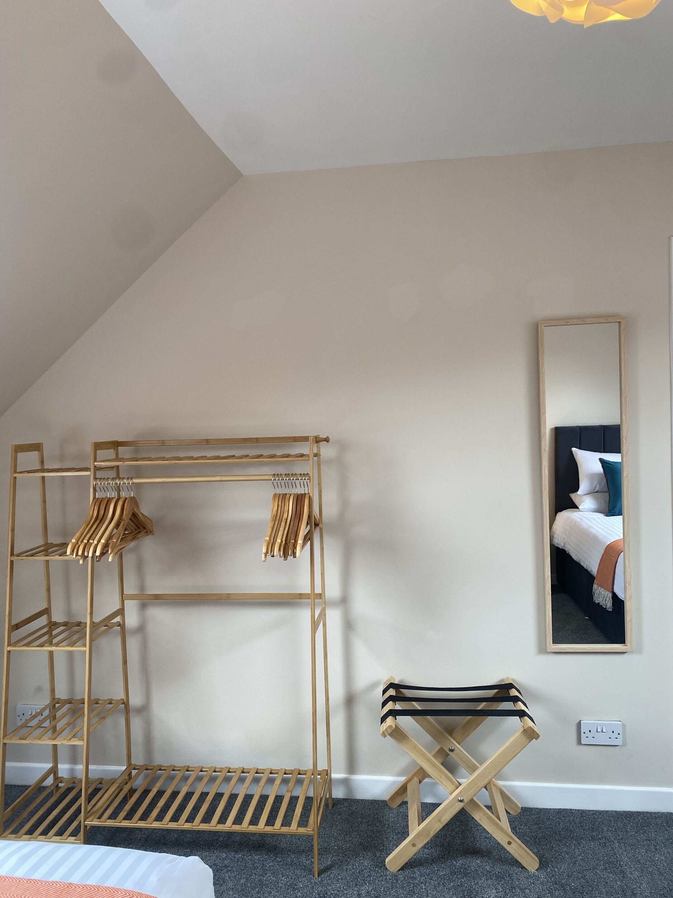Um quarto com uma cama de solteiro e beliche, um banco de madeira, um espelho e uma estante.