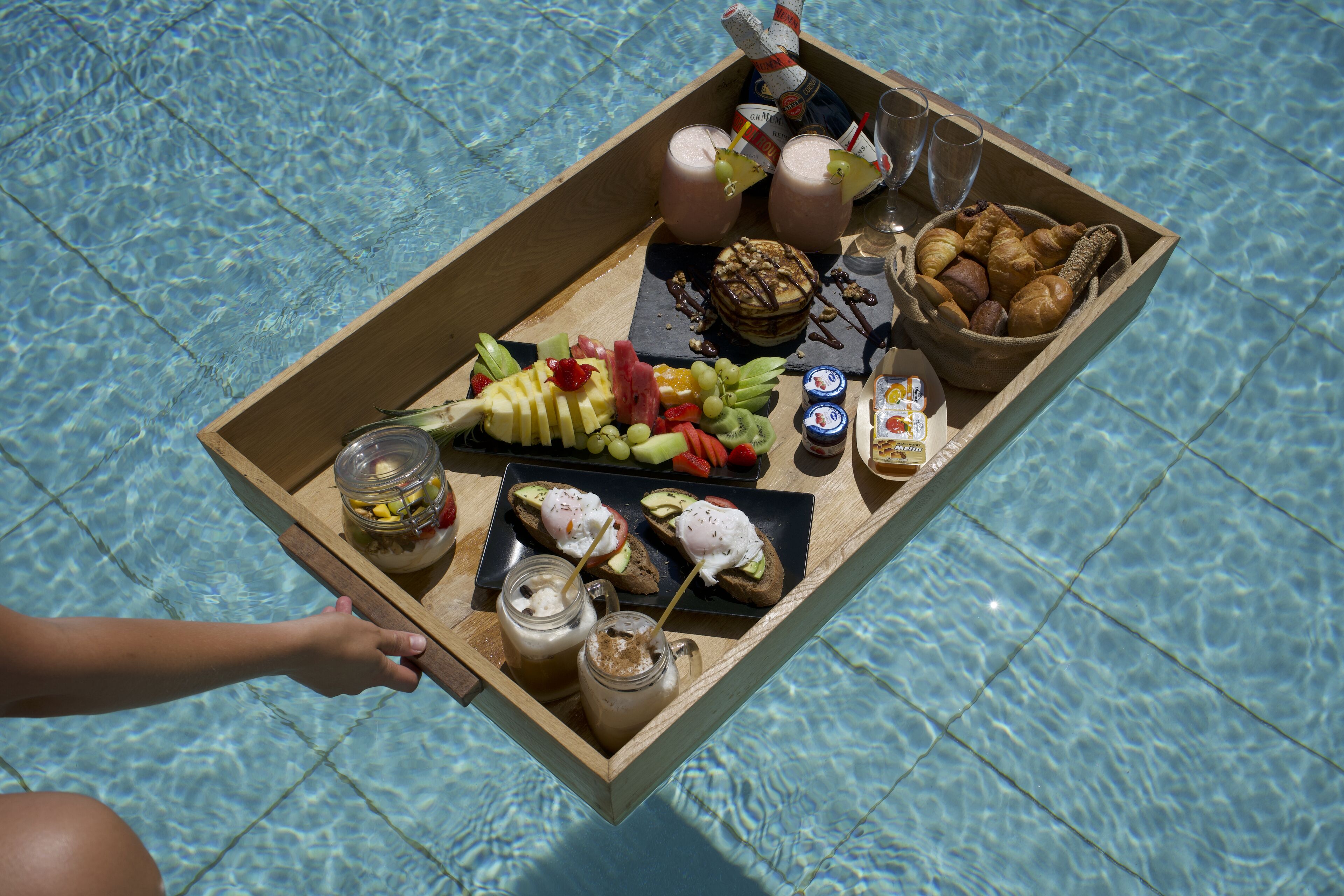 Uma bandeja com comida e bebidas ao lado de uma piscina.