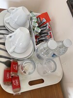 Uma bandeja com chávenas brancas, pires, embalagens de Nescafé Original, garrafas de água e bolachas Lotus.