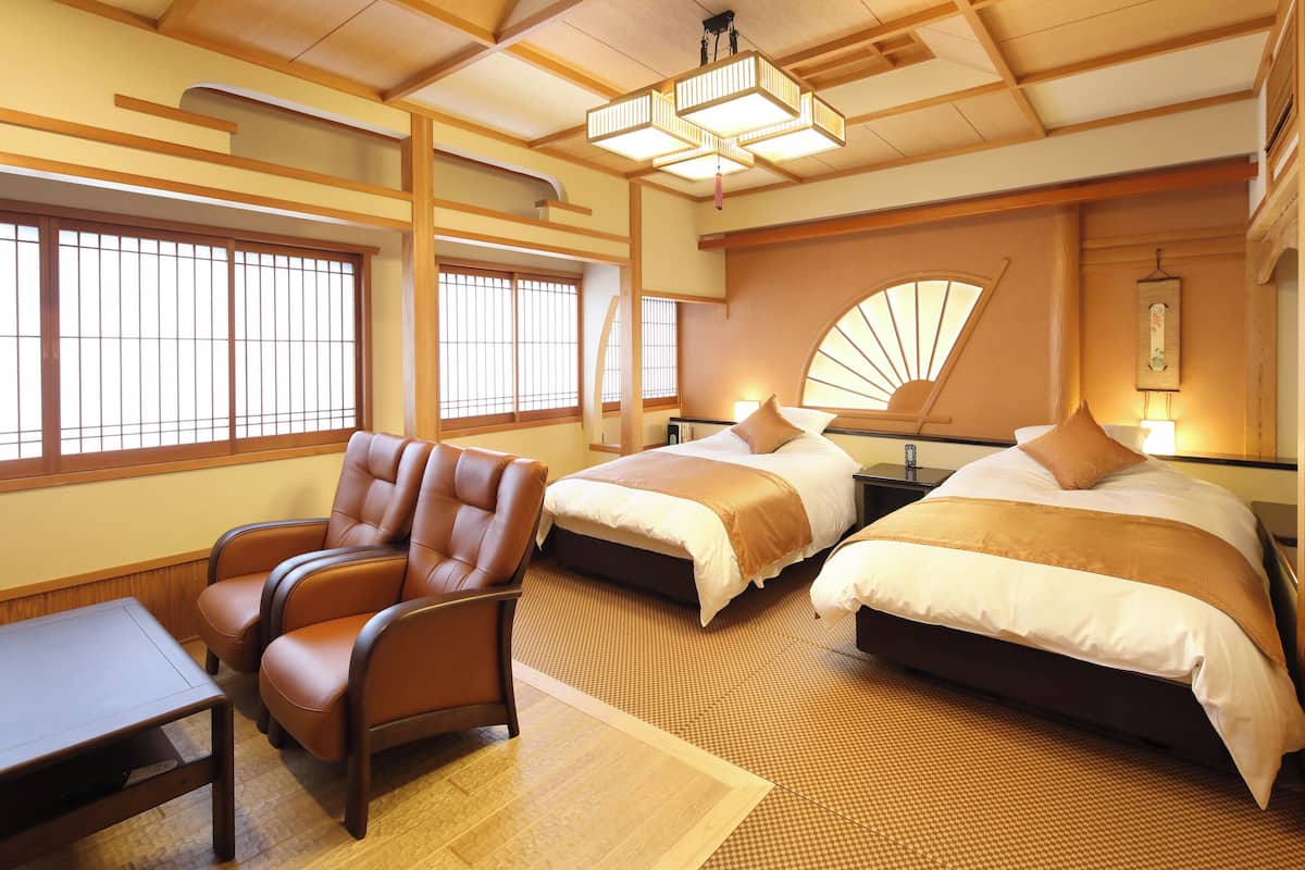 Quarto de hotel no estilo tradicional japonês com duas camas, um espaço de estar com uma poltrona e uma janela grande com vista.