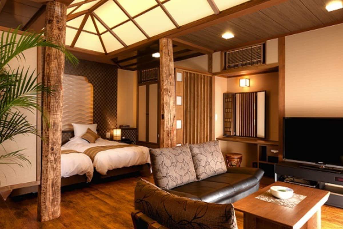 Quarto de hotel com cama, sofá, televisão e piso de madeira.