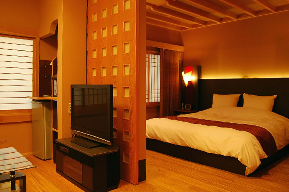 Quarto de hotel com cama, televisão, escrivaninha e guarda-roupa.