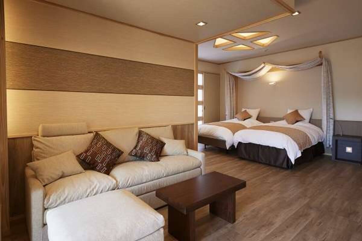 Quarto de hotel com sofá, cama, mesa de cabeceira e piso de madeira.