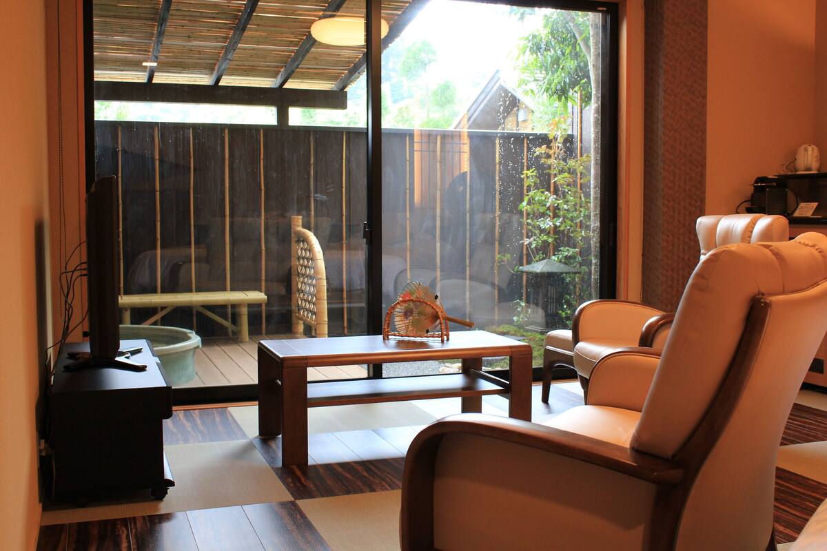 Uma sala de estar moderna com uma porta de vidro deslizante que dá para um deck, uma mesa de madeira e duas poltronas de couro.
