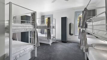 Quarto com beliches, ventoinha no teto e uma grande janela com cortinas.