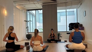 Aula de yoga num estúdio moderno com grandes janelas, soalho de madeira e decoração minimalista.