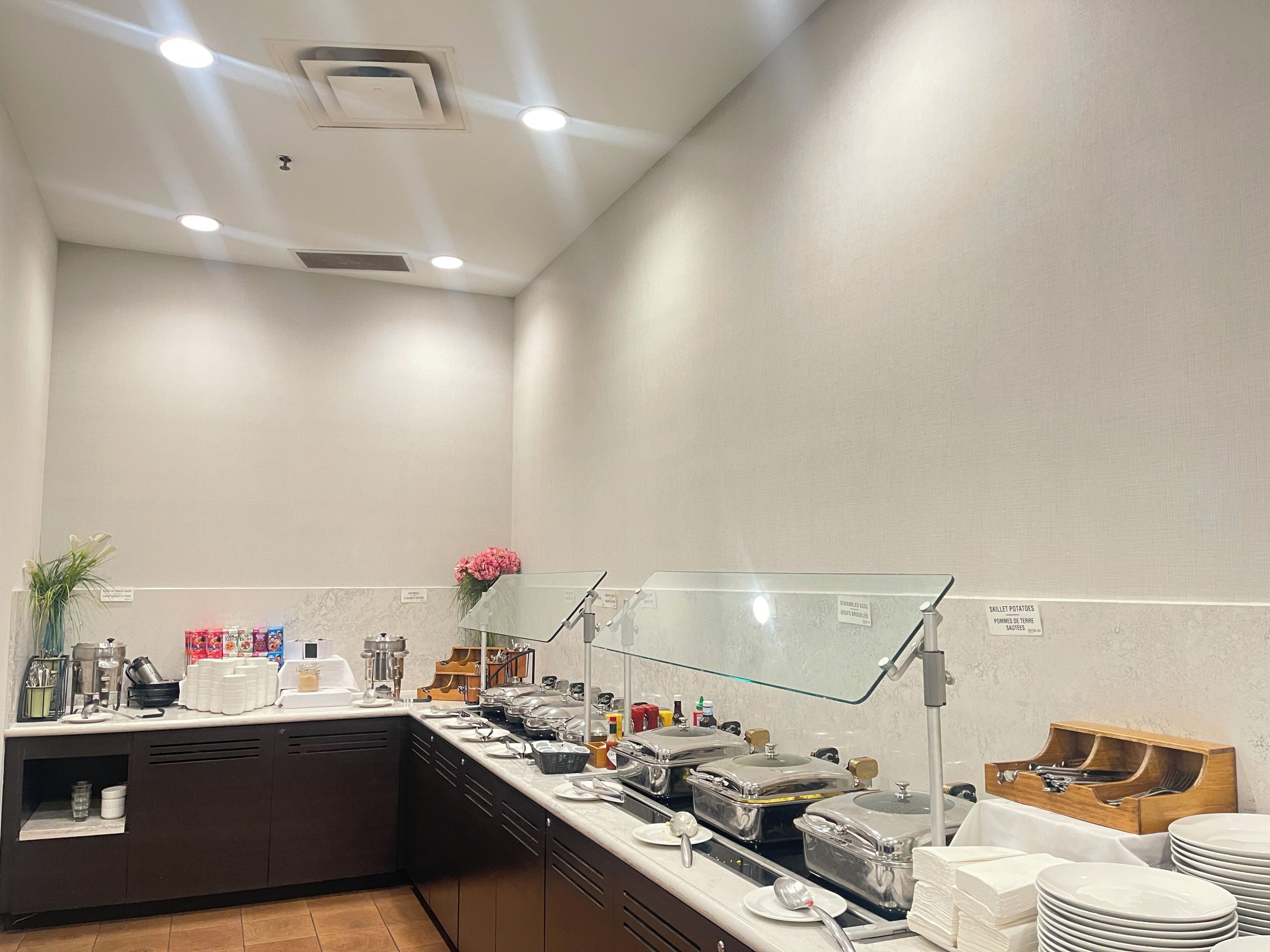 Disposição de buffet com recipientes de comida, utensílios de servir e uma divisória de vidro.