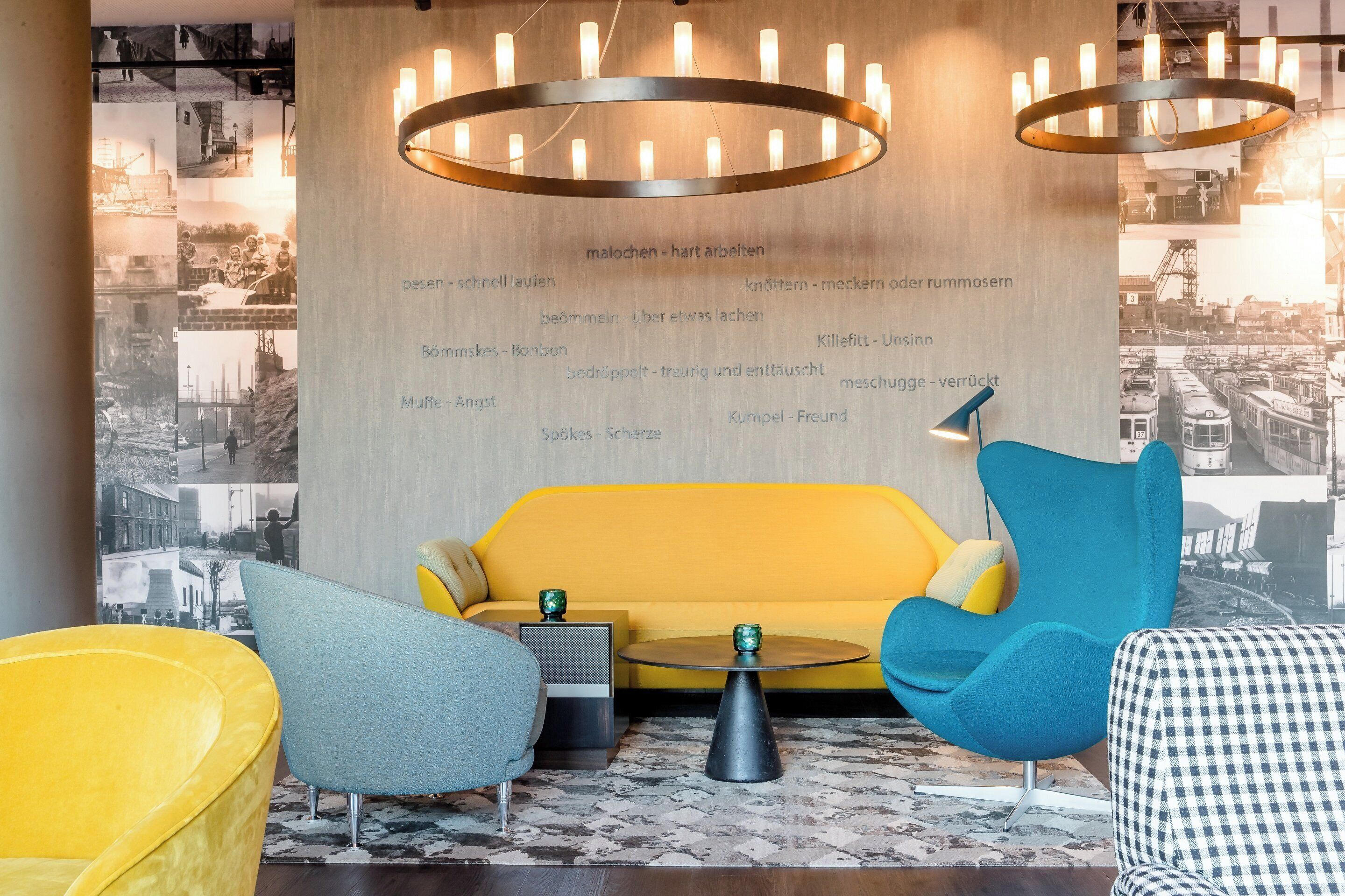 Um lounge moderno com um sofá amarelo, poltronas azuis e uma mesa de centro redonda.
