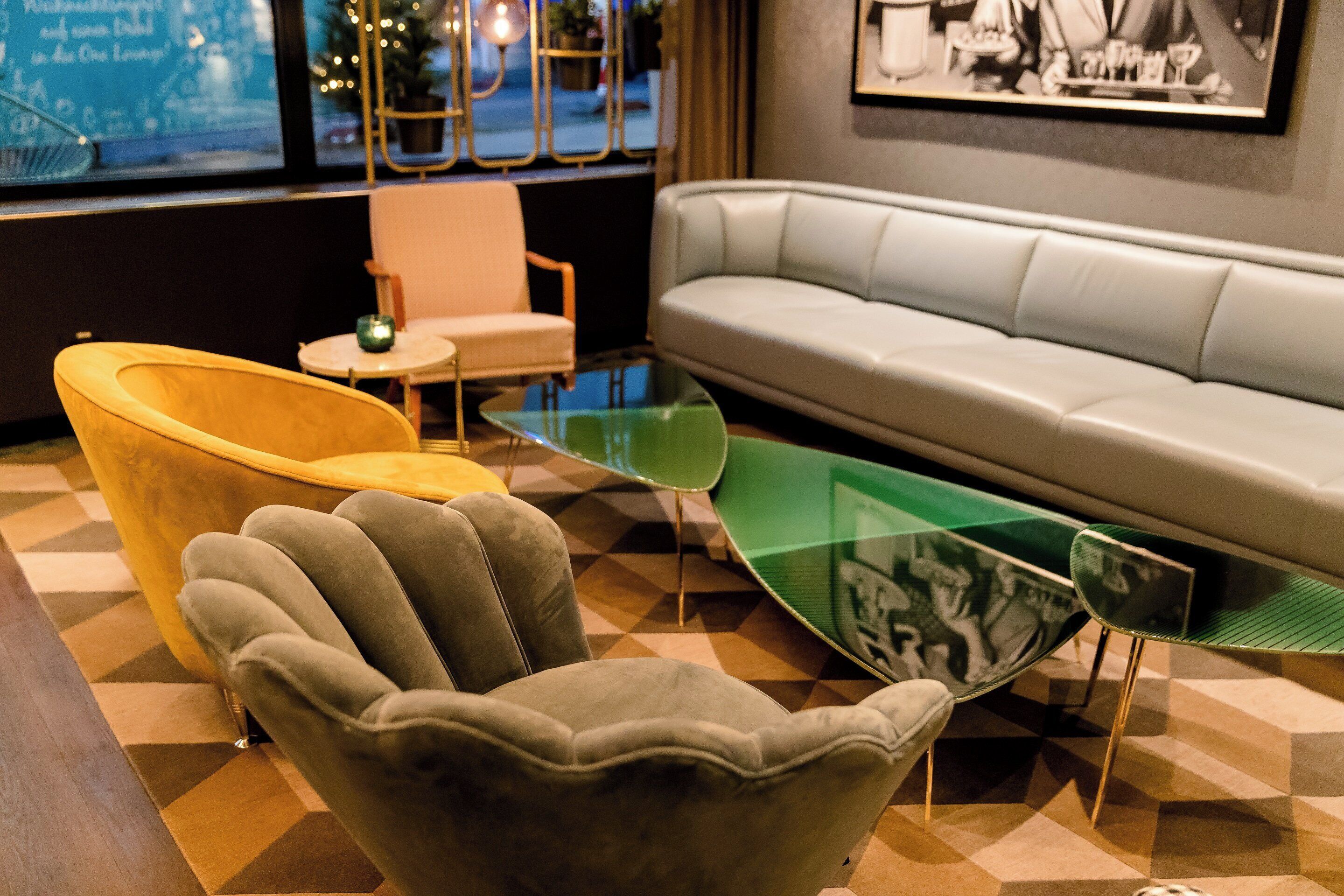 Uma área de estar moderna com um sofá cinzento, uma poltrona amarela e uma mesa de vidro verde.